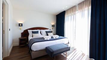 Quarto de hotel moderno com uma cama grande, mesas de cabeceira e vista para o exterior.