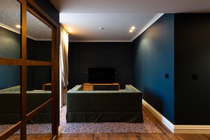Quarto moderno com parede azul escura, piso de madeira, sofá verde e televisão de tela plana fixada na parede.