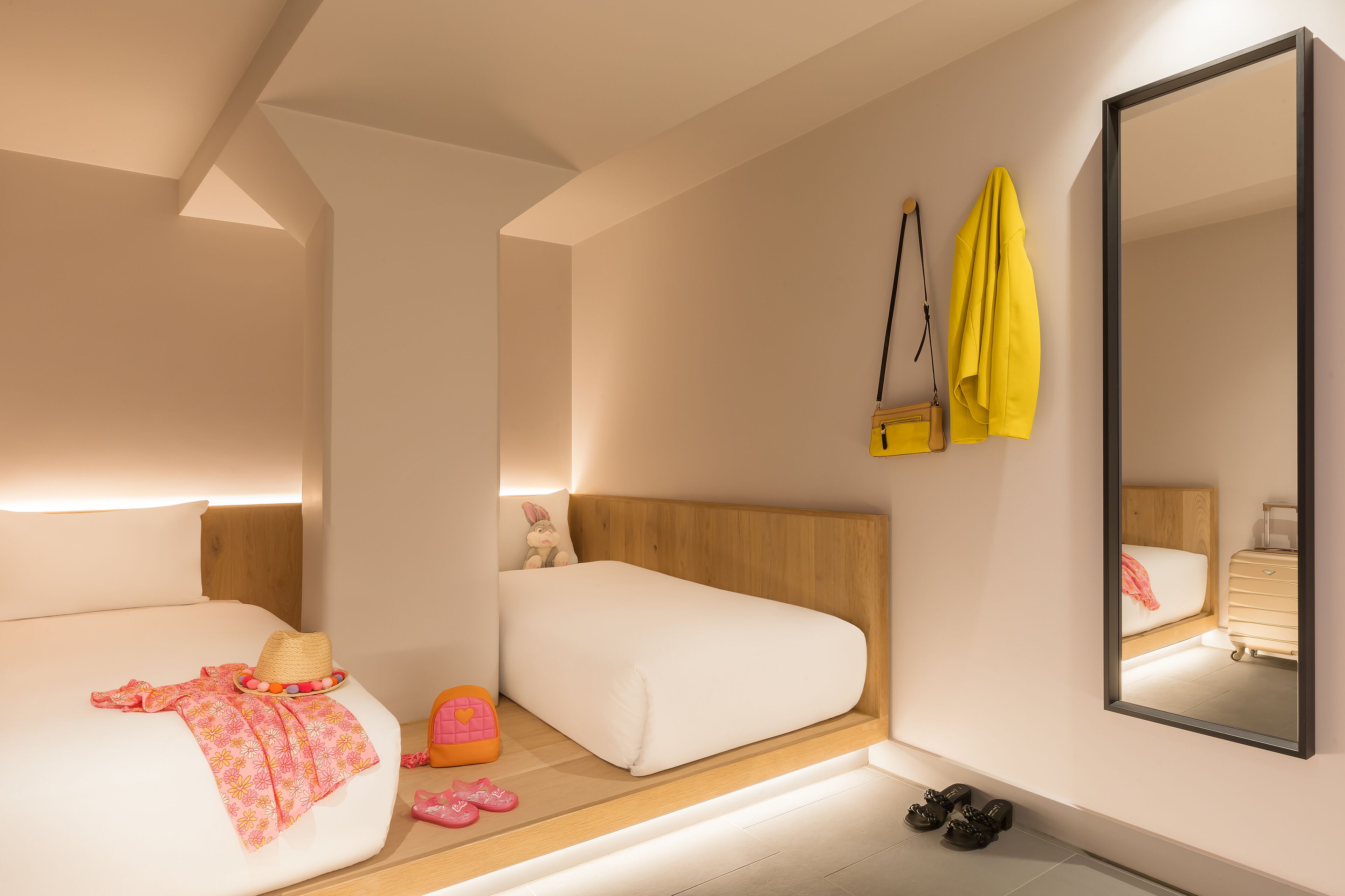 Quarto de hotel moderno com duas camas, um espelho grande e cabeceira de madeira.