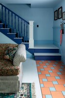 Sala de estar com escada azul, sofá estampado com flores, poltrona listrada e tapete padronizado.