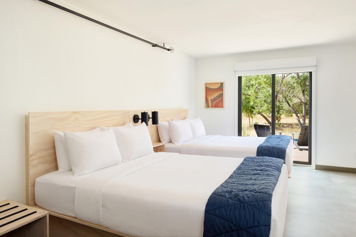 Quarto de hotel com duas camas, uma janela grande e vista para o exterior.