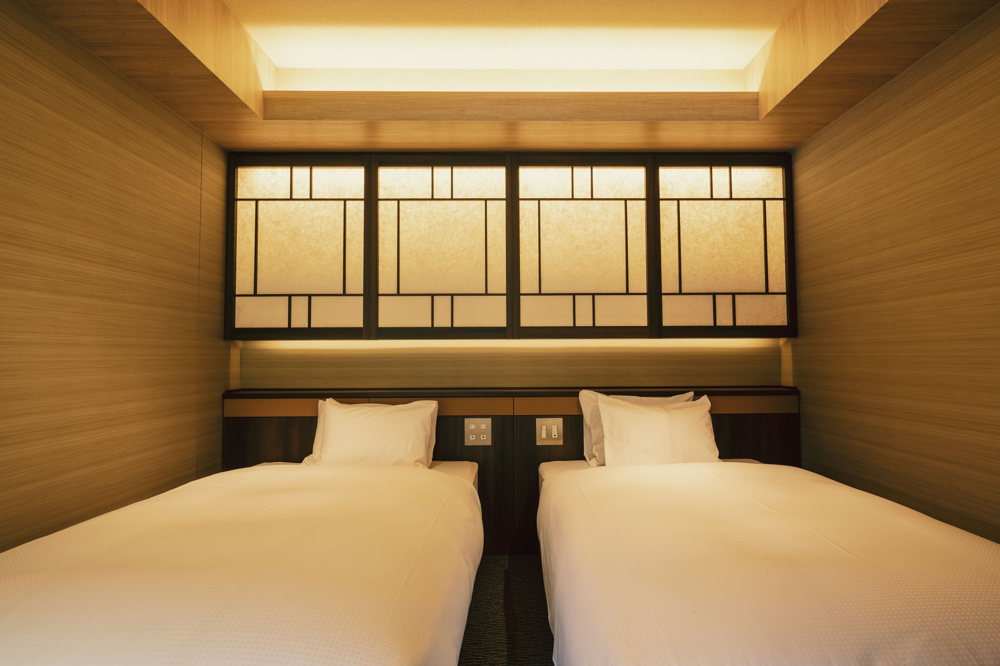 Quarto de hotel com duas camas, um claraboia e uma cabeceira de madeira.