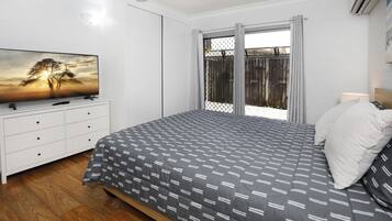 Quarto com cama, televisão, penteadeira e janela com cortinas.