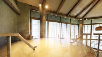 Uma onsen japonesa tradicional com uma grande fonte termal circular rodeada por vigas de madeira e esteiras de tatame.