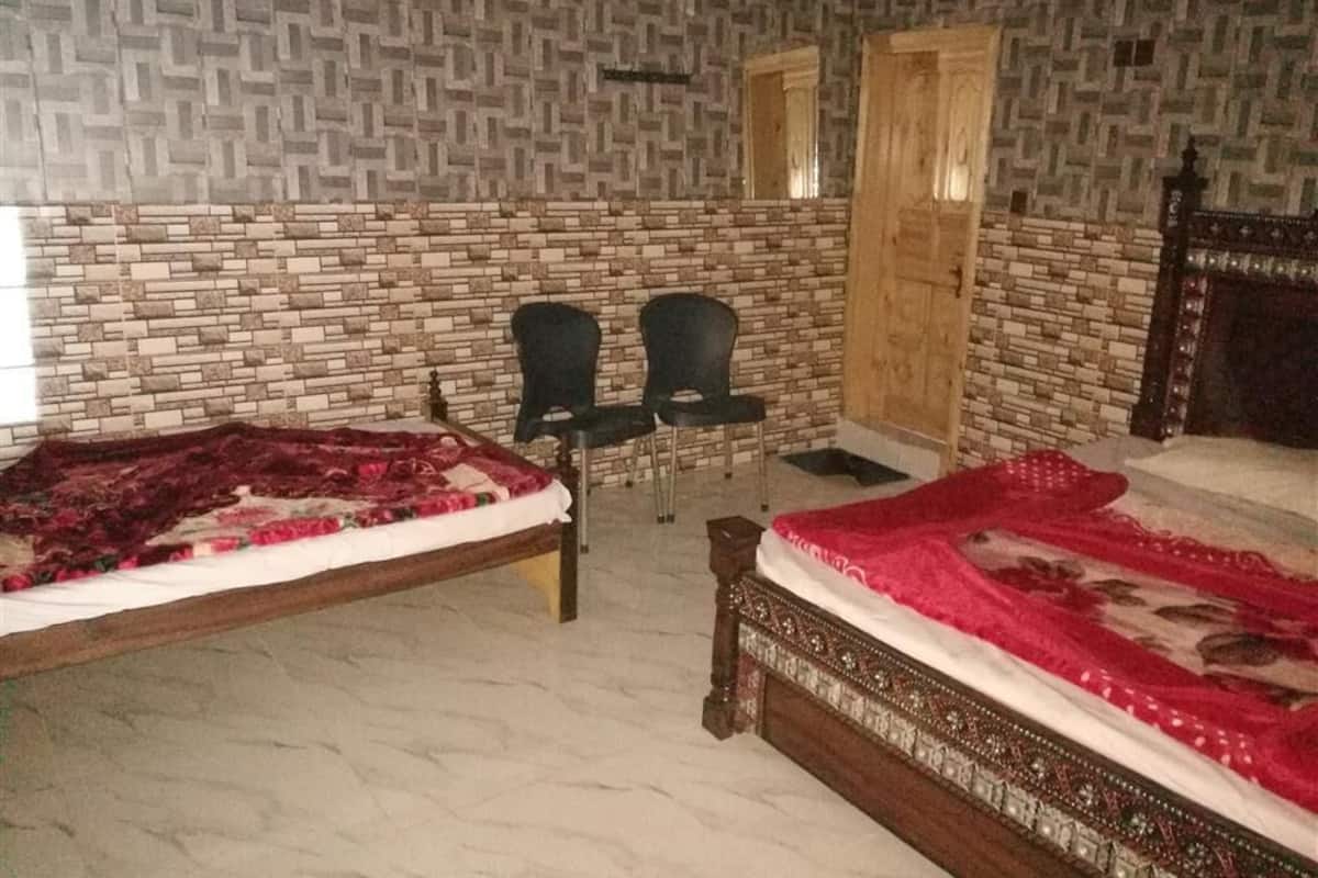 Quarto com duas camas, parede com padrão de tijolos e duas portas de madeira.