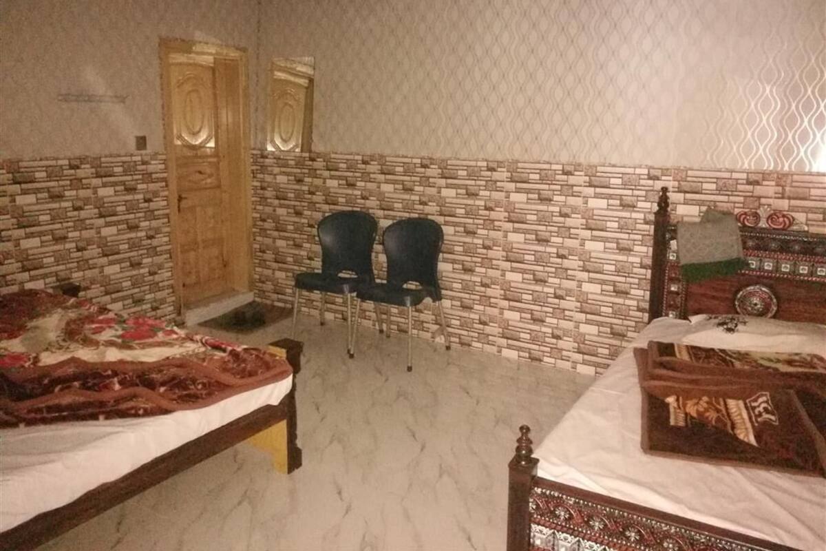 Quarto com duas camas, um guarda-roupa de madeira, duas cadeiras e papel de parede estampado.