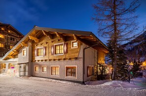 Um edifício em estilo cabana de tronco com várias janelas e telhado inclinado, rodeado de neve e árvores.