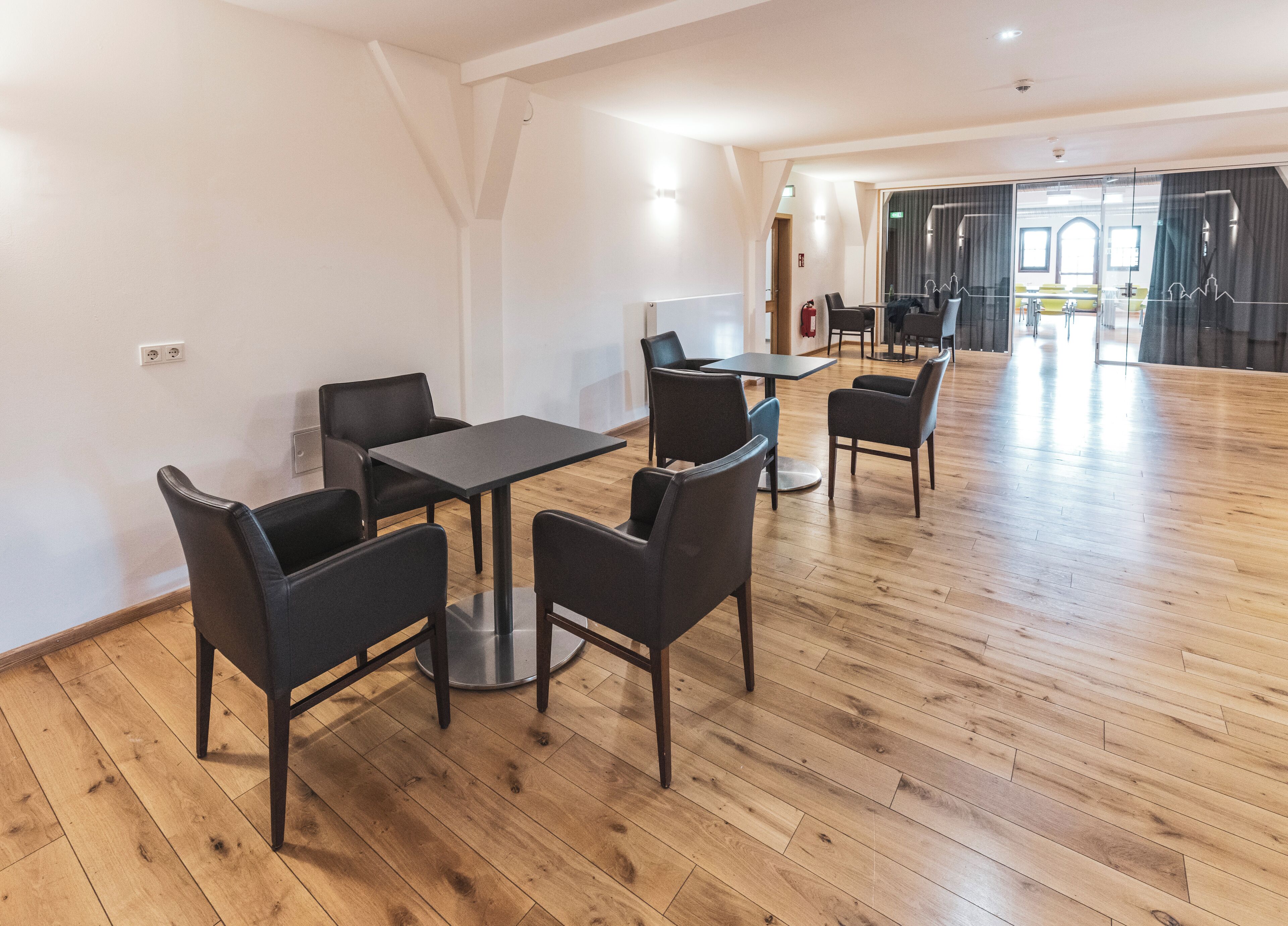 Um quarto espaçoso com assoalho de madeira, uma mesa de jantar com cadeiras e uma janela grande com cortinas.