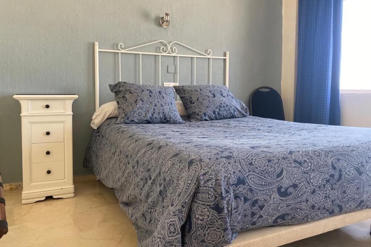 Quarto com uma cama, mesa de cabeceira e luminária na parede.
