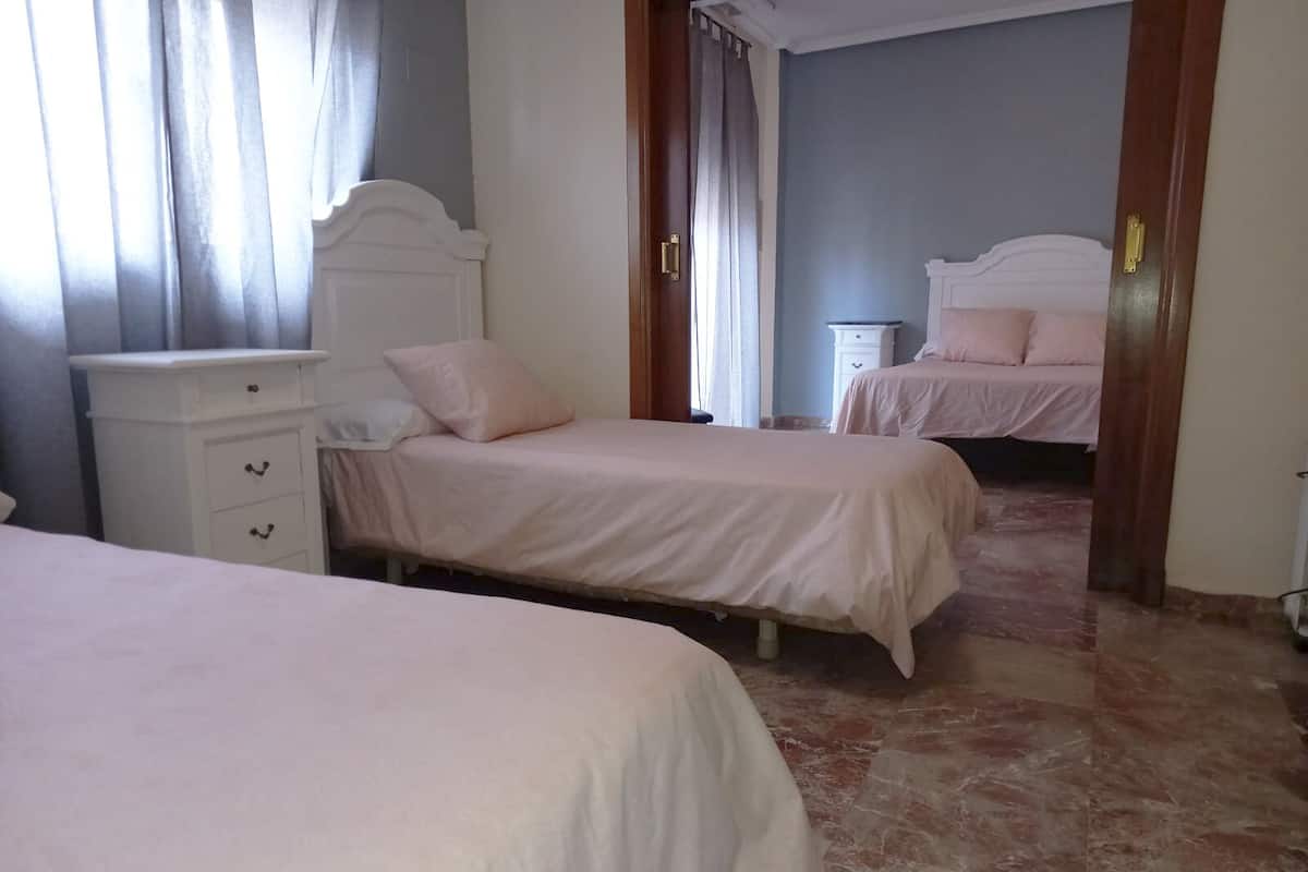 Quarto com duas camas de solteiro, uma cômoda branca e uma mesinha de cabeceira.