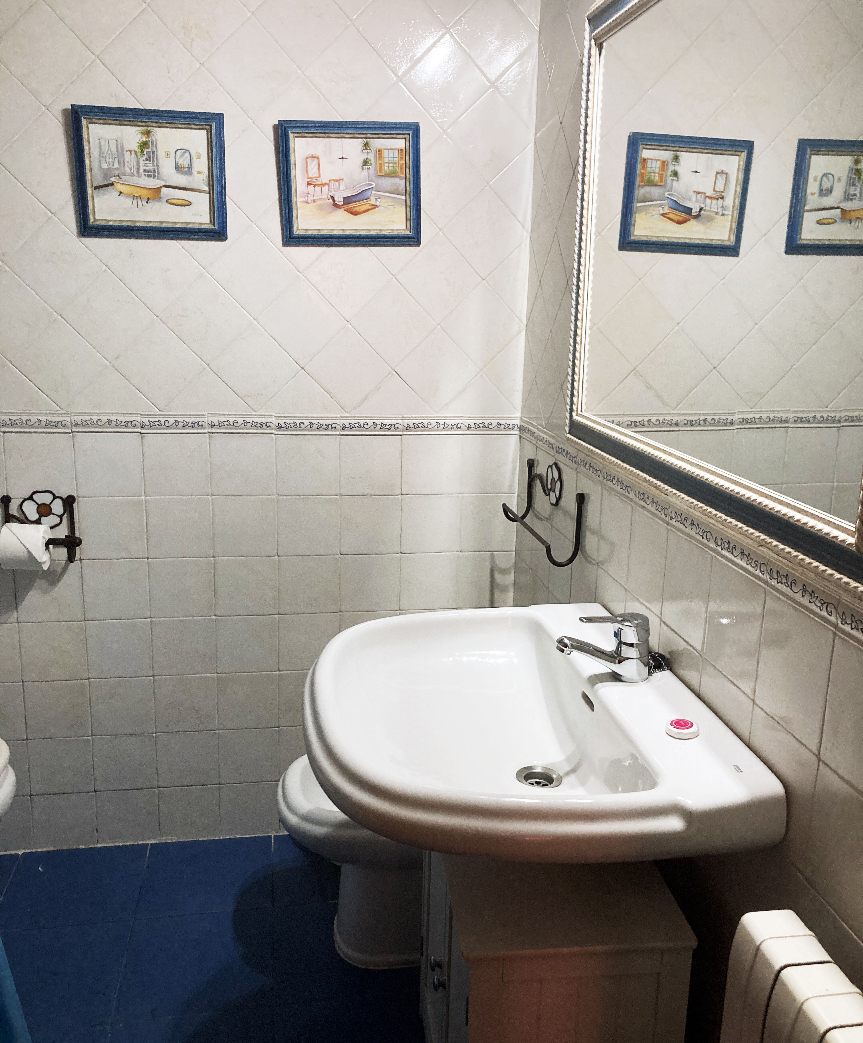 Casa de banho com lavatório branco, espelho e três quadros na parede.