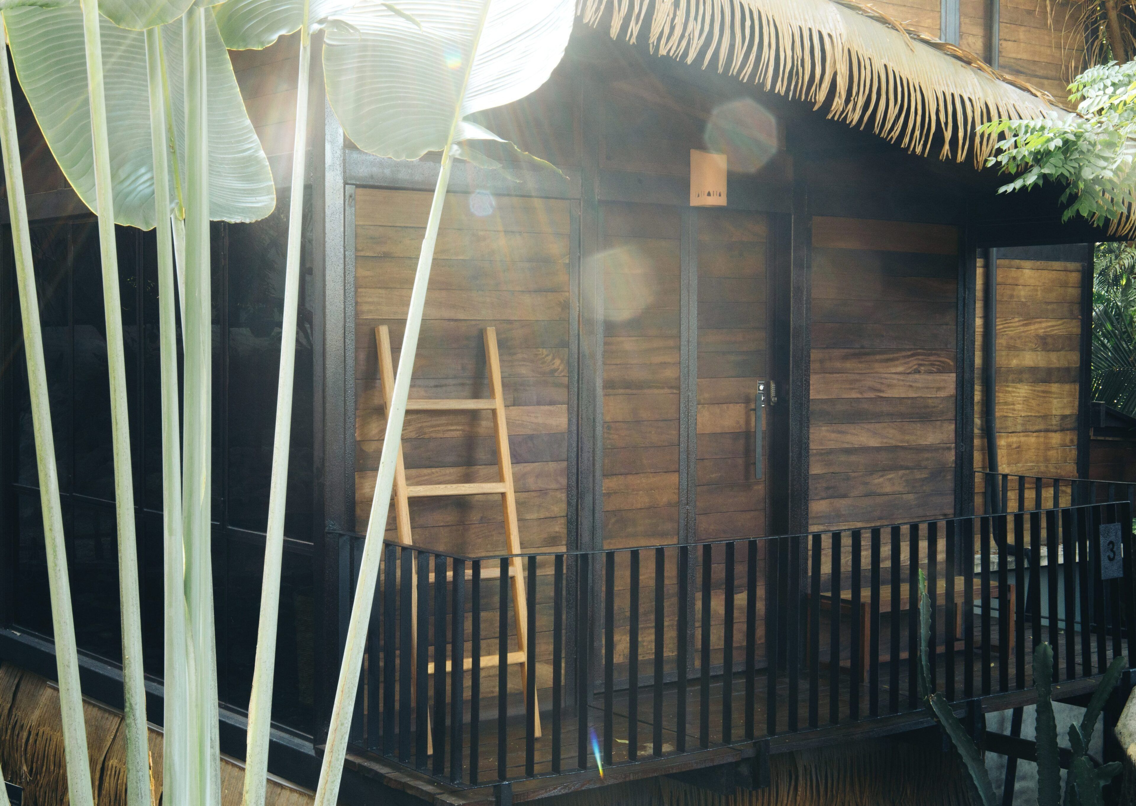 Uma cabana de madeira com telhado de palha, um deck de madeira e uma escada que leva à porta.