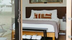 Quarto com cama, janela e vista para árvores.