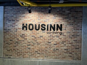 Paredes de tijolo com o texto "HOUSINN co-living" em letras grandes e negrito.