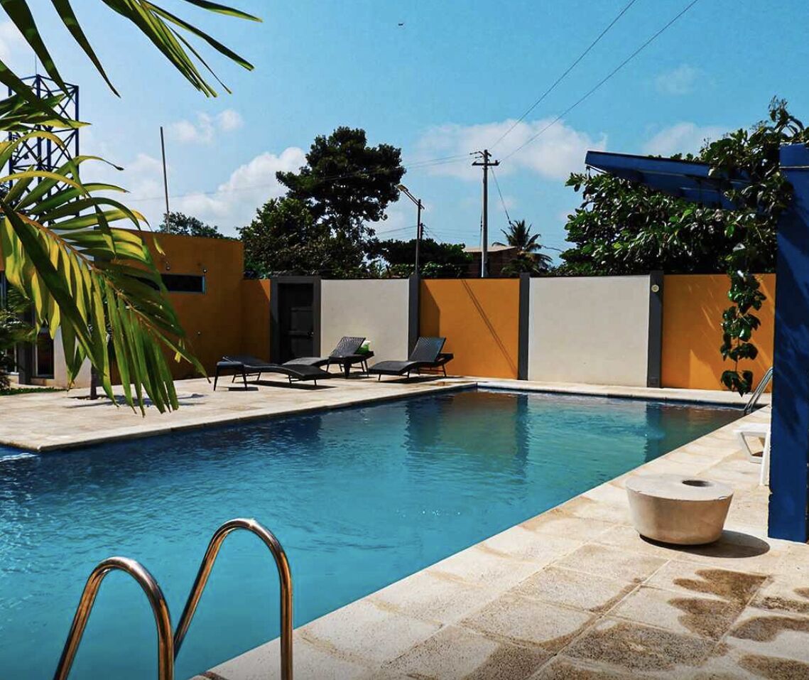 Piscina com espreguiçadeiras, um deck de concreto e um edifício moderno ao fundo.