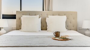 Cama bem arrumada com um edredom cinzento, duas almofadas brancas e uma bandeja de madeira com uma caneca e uma tigela de comida.
