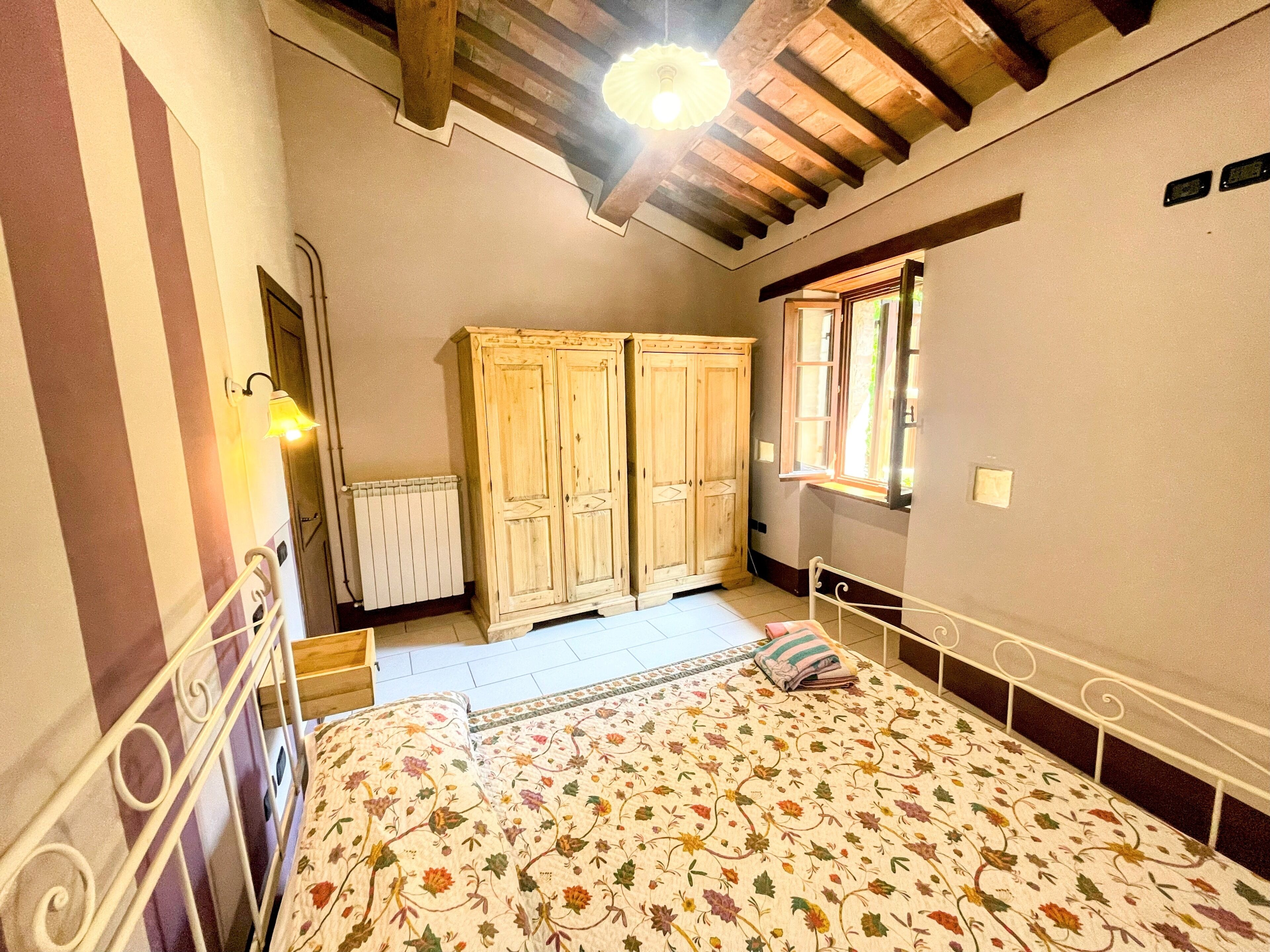 Quarto com cama, guarda-roupa de madeira, radiador e janela com vista.
