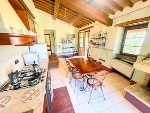 Uma cozinha com mesa de madeira, cadeiras, fogão a gás e geladeira.
