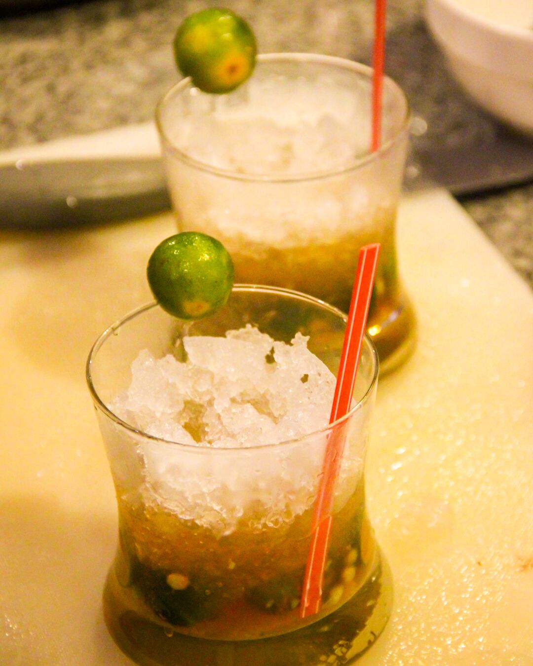 Dois copos com gelo e rodelas de limão, possivelmente contendo um coquetel, sobre uma mesa.