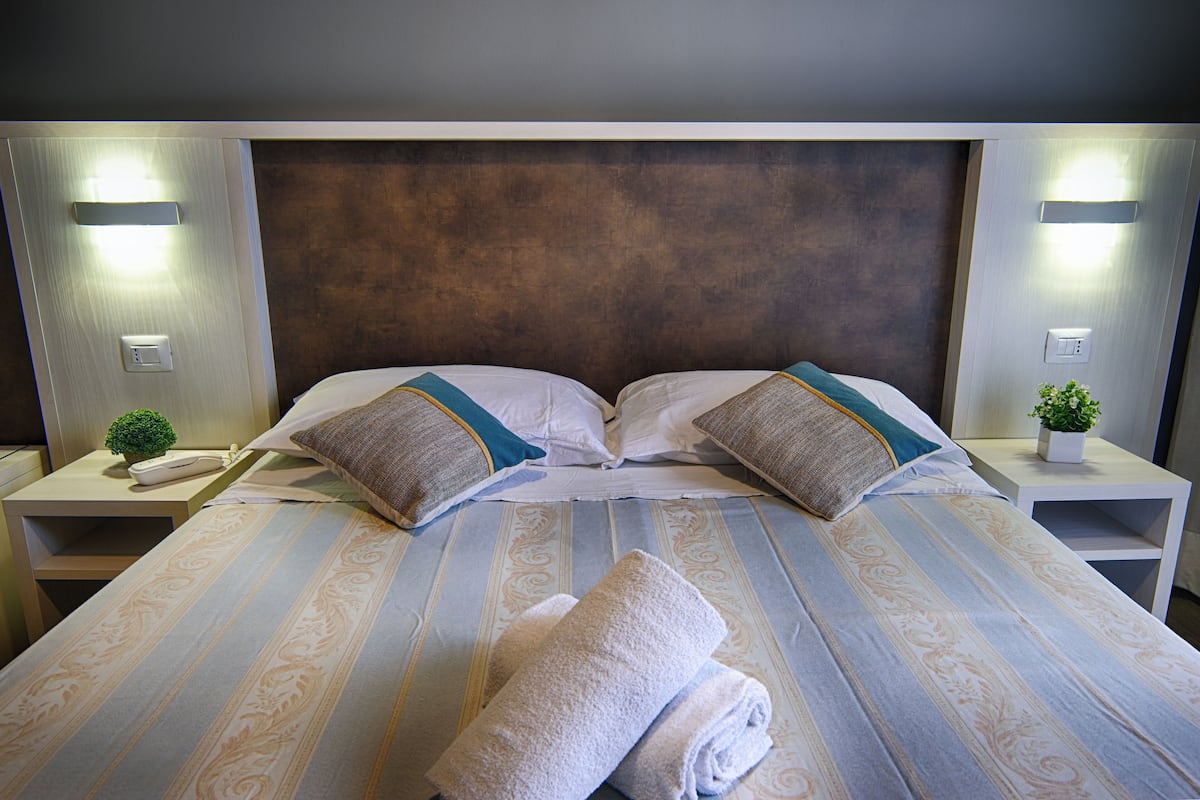 Uma cama de casal bem arrumada, com roupa de cama listrada, duas almofadas e uma toalha dobrada.