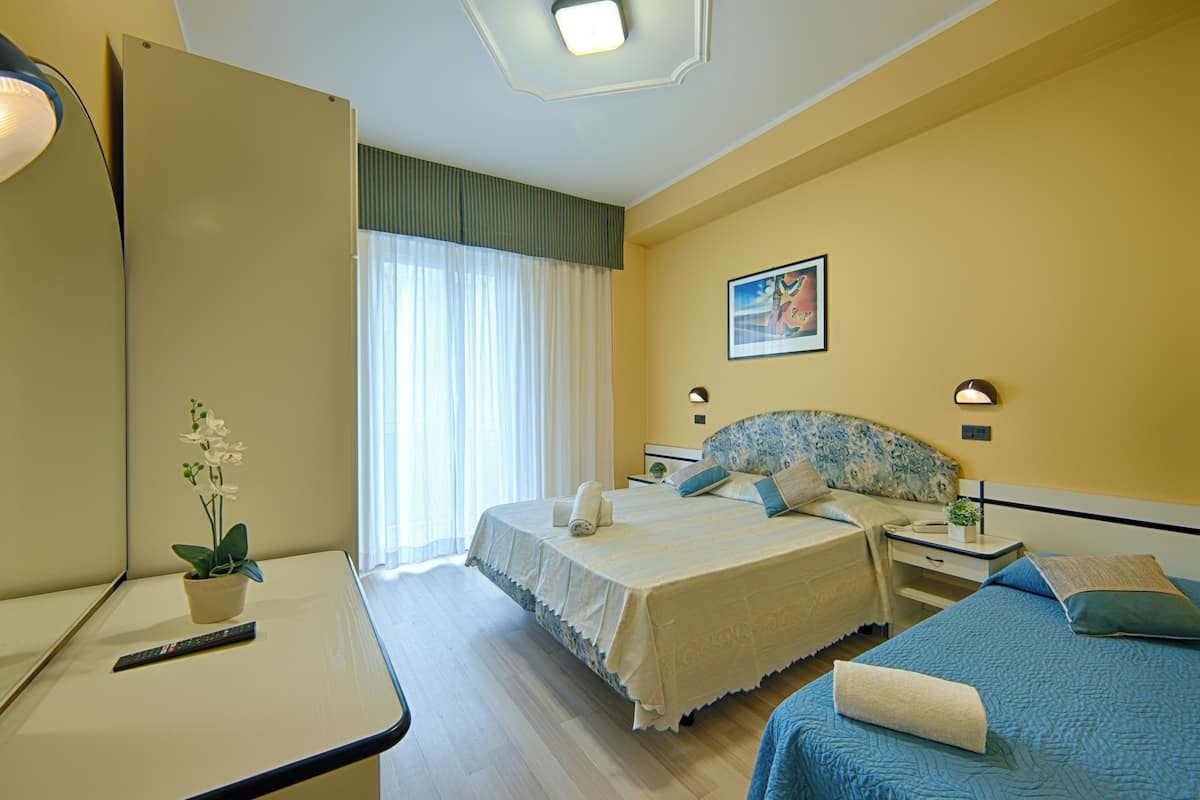 Quarto de hotel com uma cama, mesas de cabeceira, abajur, planta em vaso e um quadro na parede.