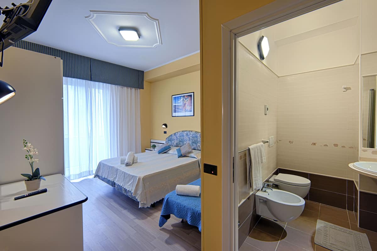Quarto de hotel com cama, mesa de cabeceira e banheiro com vaso sanitário, bidê e pia.