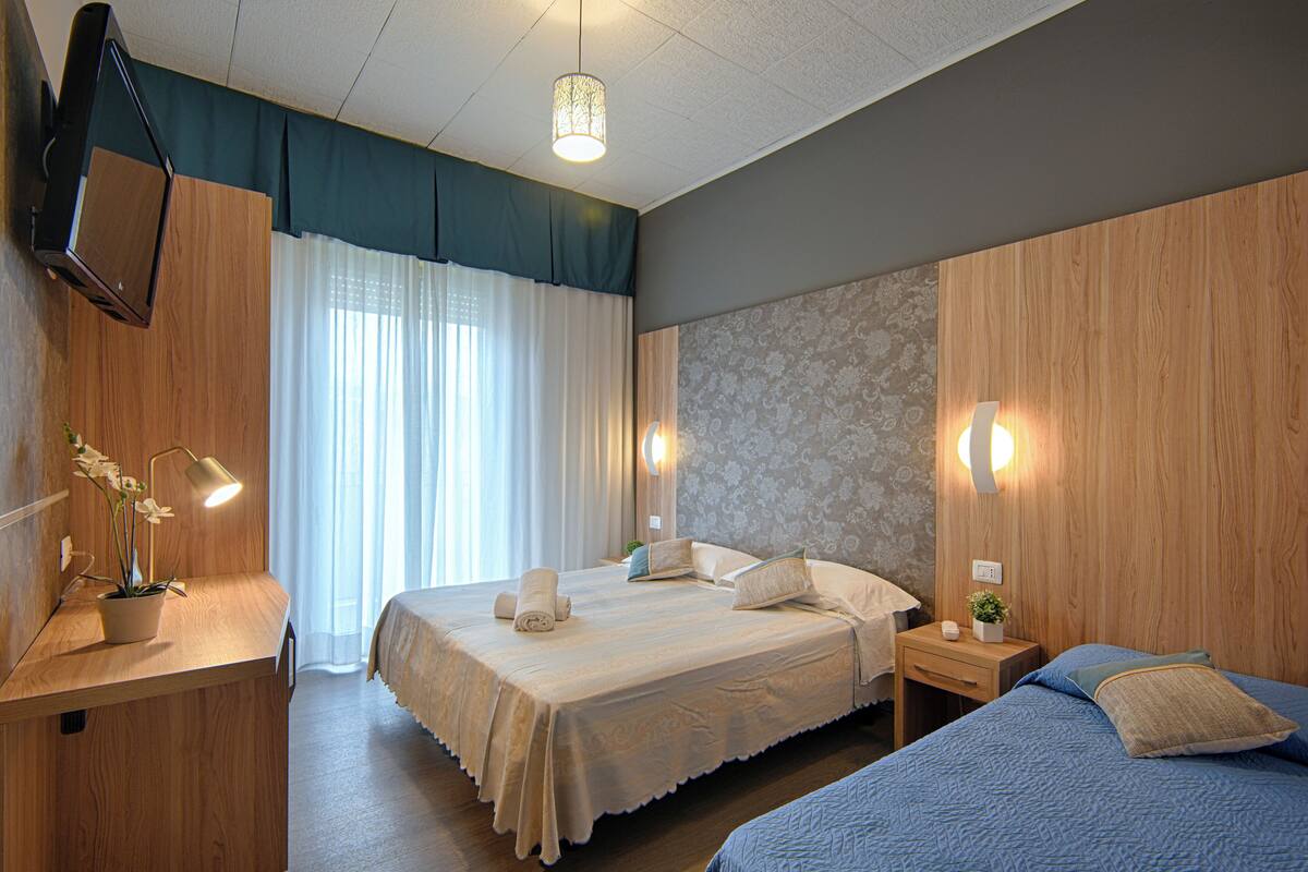 Quarto de hotel com duas camas, uma escrivaninha, uma televisão e uma janela com cortinas.