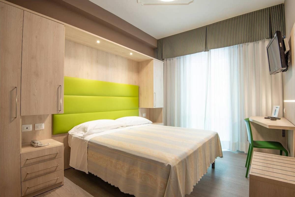 Quarto de hotel com uma cama, uma escrivaninha, uma cadeira e uma televisão.