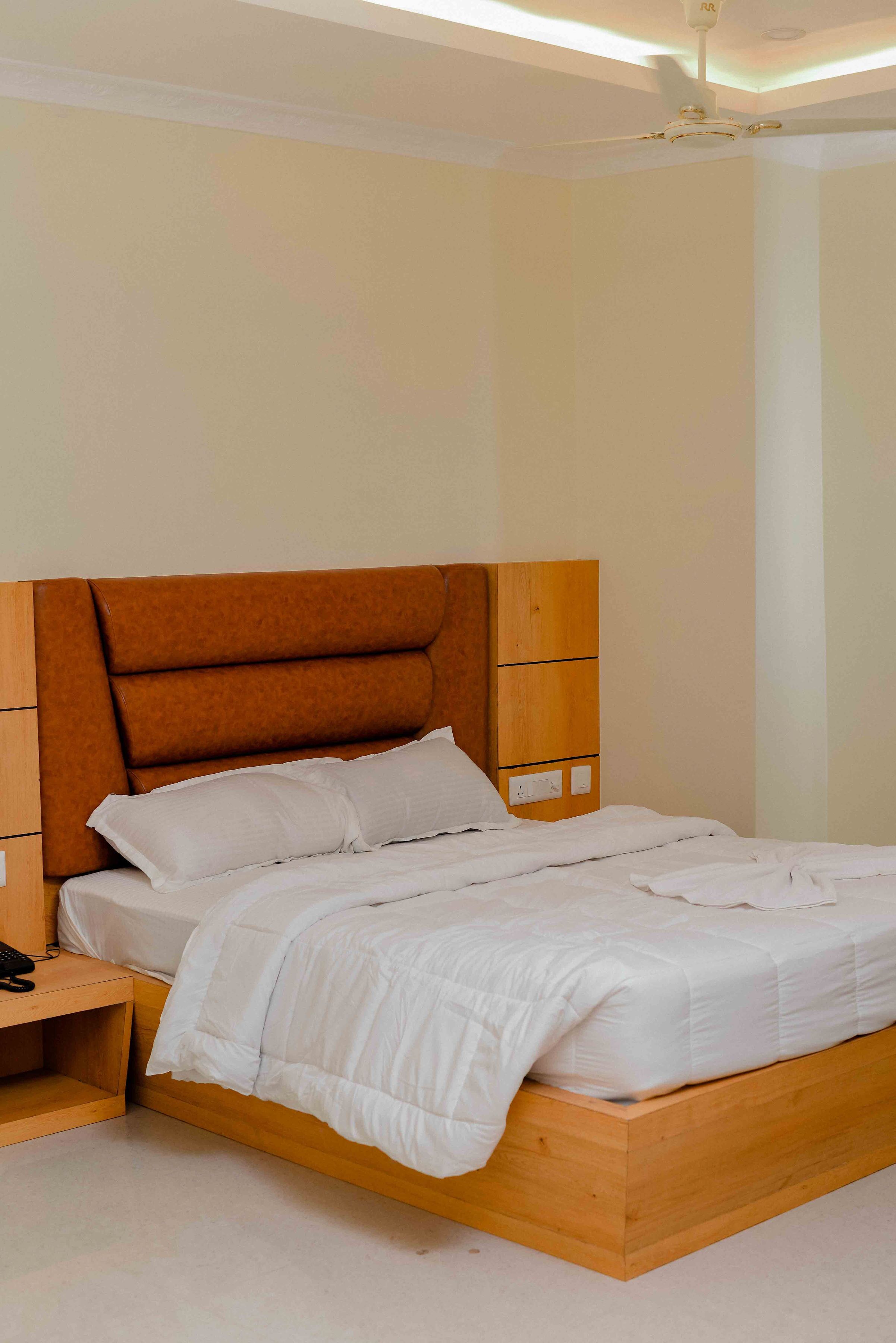 Uma cama bem arrumada com cabeceira de madeira, uma mesa de cabeceira com abajur e um ventilador de teto.