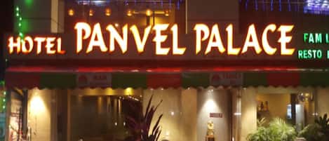 Exterior do Hotel Panvel Palace com um letreiro de neon, um bar e mesas ao ar livre.