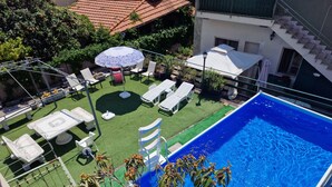 Piscina com um terraço ensolarado, incluindo cadeiras de descanso e uma mesa com guarda-sol.