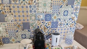 Cozinha com painel de azulejos, exibindo diversos padrões e cores. Há uma cafeteira, uma chaleira e um pote sobre o balcão.