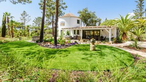 Uma casa branca com telhado de cerâmica, rodeada por um gramado bem cuidado e diversas plantas.