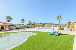 Uma área de piscina em resort, com várias piscinas, espreguiçadeiras e palmeiras.