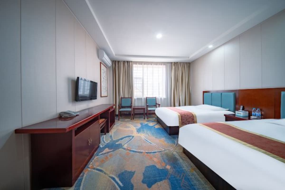 Quarto de hotel com cama, escrivaninha, televisão e janela com cortinas.