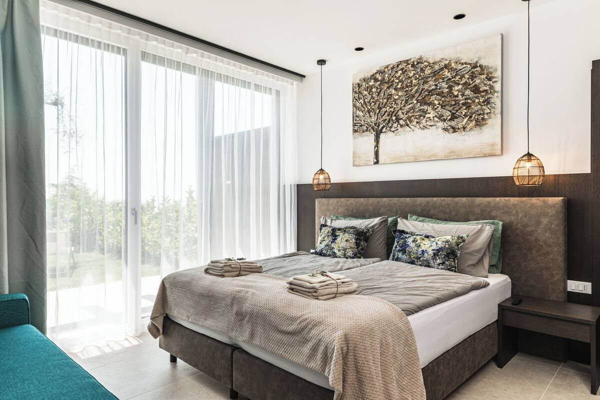 Um quarto moderno com uma cama grande, uma mesinha de cabeceira, um sofá e um quadro na parede.