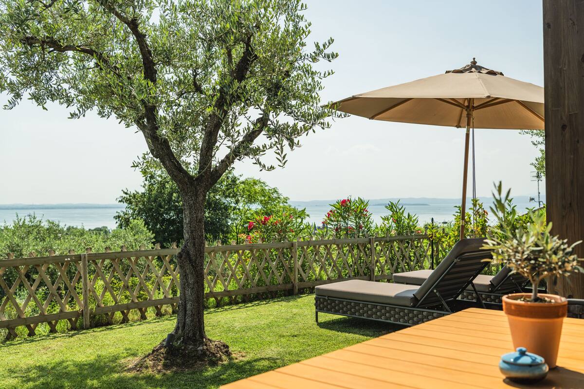 Um deck de madeira com uma mesa, uma poltrona de descanso e um guarda-sol.