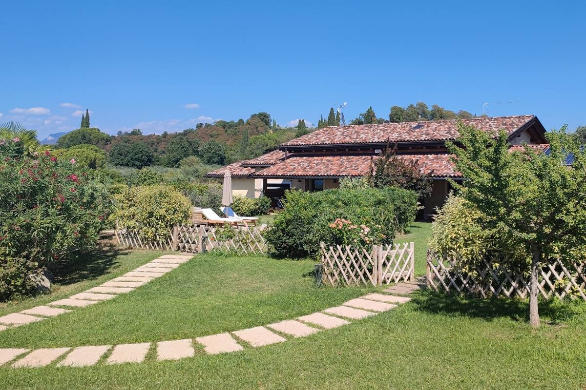 Uma villa com telhado de azulejos, rodeada por um jardim com caminho pavimentado.