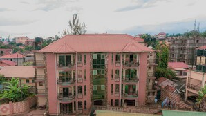 Um edifício de vários andares com varandas e janelas amplas, rodeado por outros edifícios e vegetação.