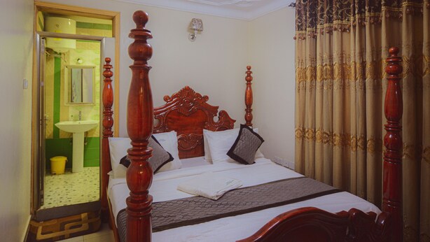 Quarto com cama de dossel, mesa de cabeceira, espelho e banheiro visível através de uma porta aberta.