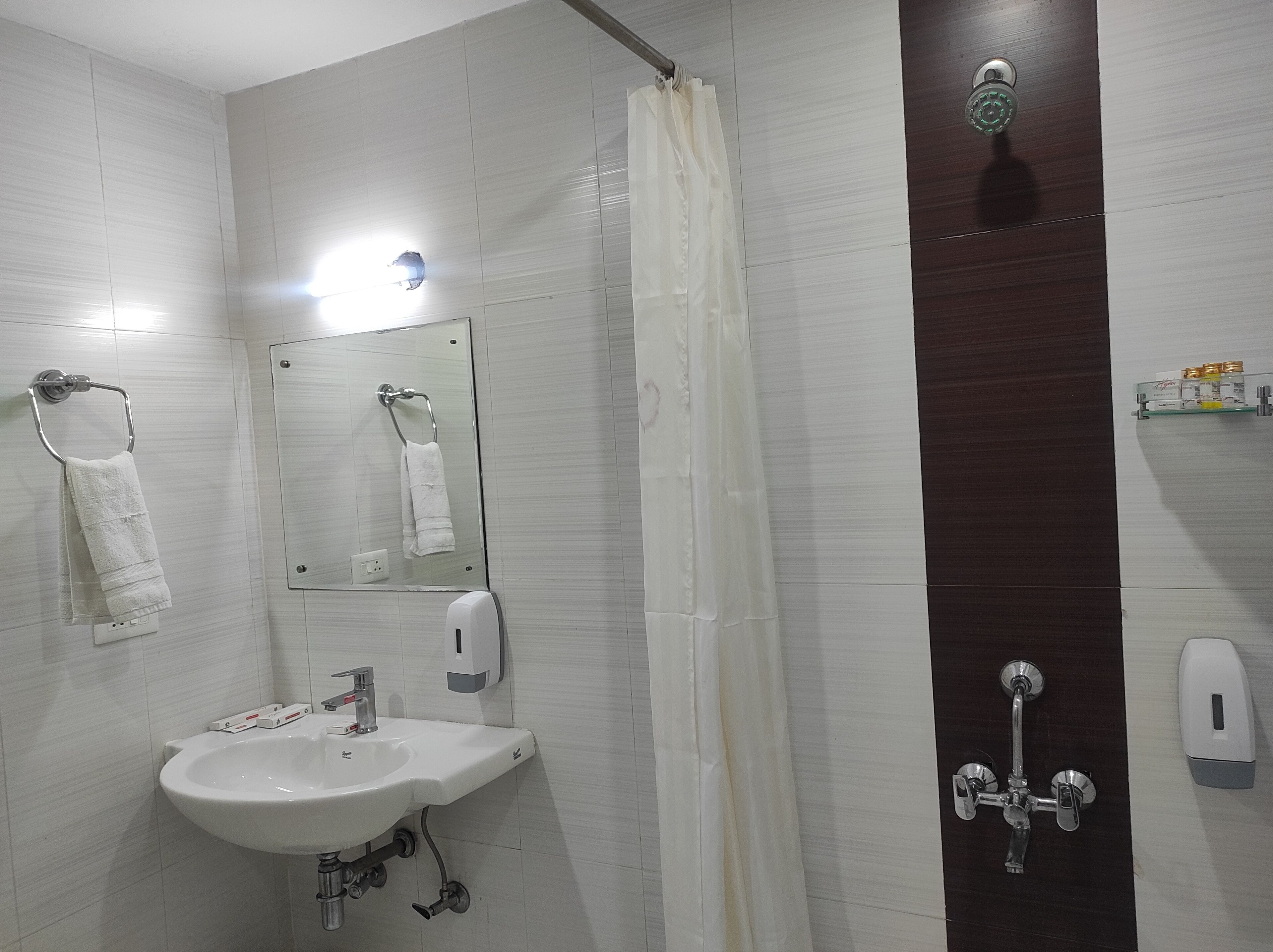 Casa de banho com lavatório branco, espelho, porta-toalhas, cortina de chuveiro e dispensador de sabonete.