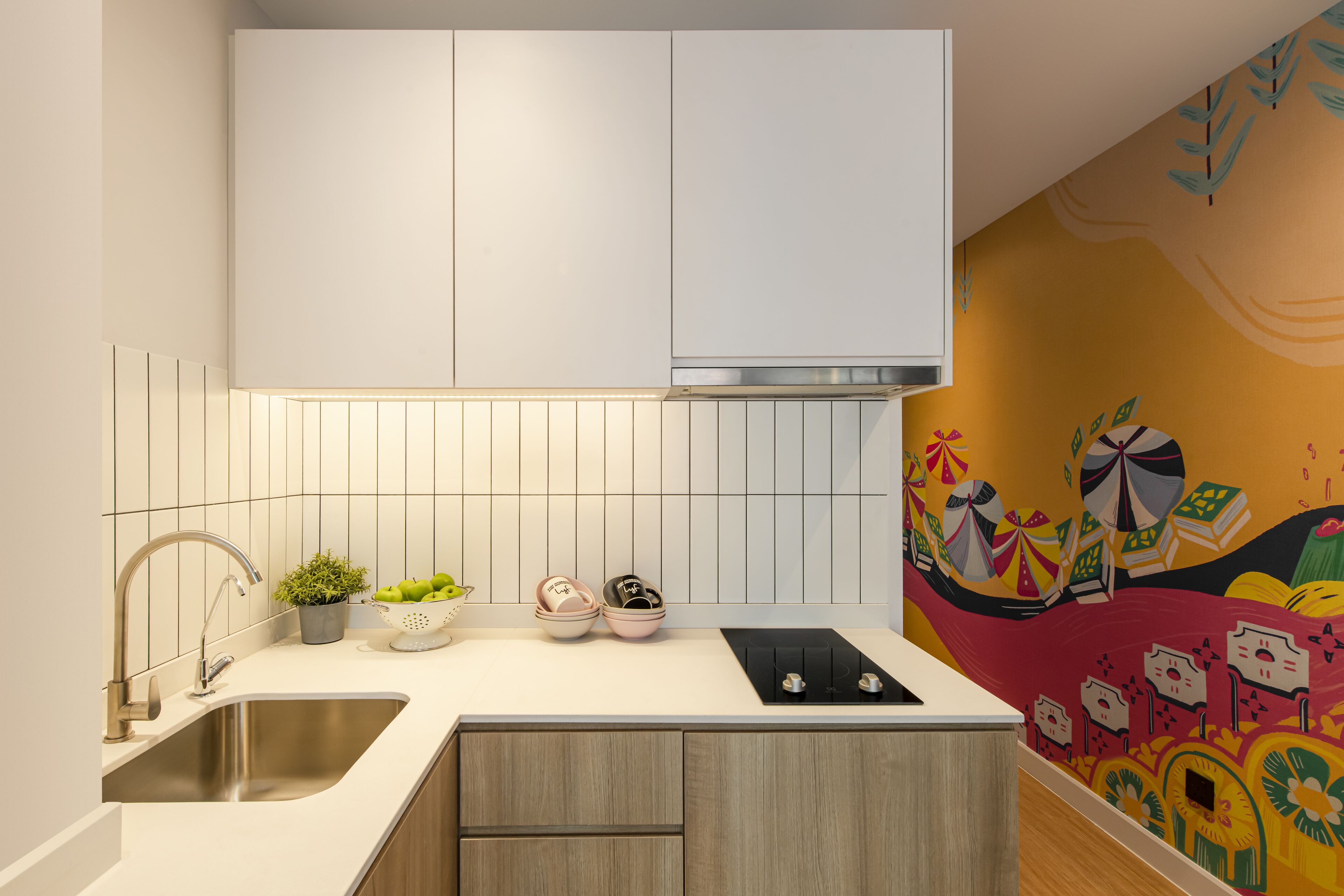 Uma cozinha moderna com armários brancos, uma pia de aço inoxidável e um mural colorido na parede.