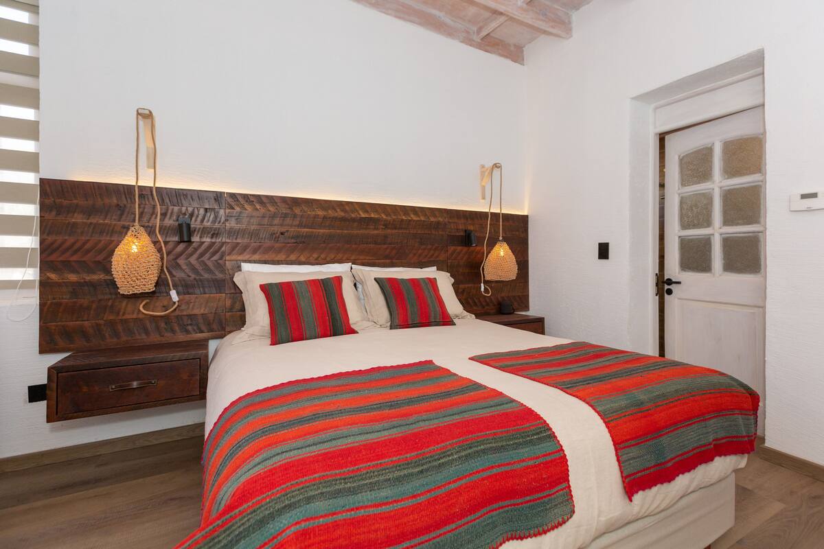 Um quarto com uma cama grande, roupa de cama listrada, cabeceira de madeira, abajures e uma porta.