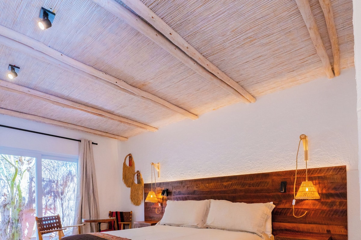 Um quarto amplo com uma cama grande, cabeceira de madeira e um banquinho.