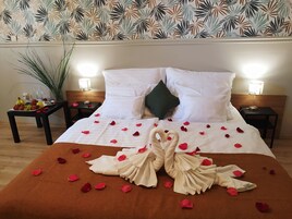 Quarto de hotel com cama bem arrumada, pétalas de rosa e arranjo de toalha em formato de cisne.