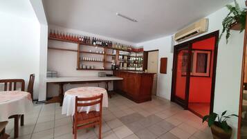 Um espaço de bar pequeno e acolhedor, com balcão de madeira, prateleiras repletas de garrafas e uma mesa com cadeiras.