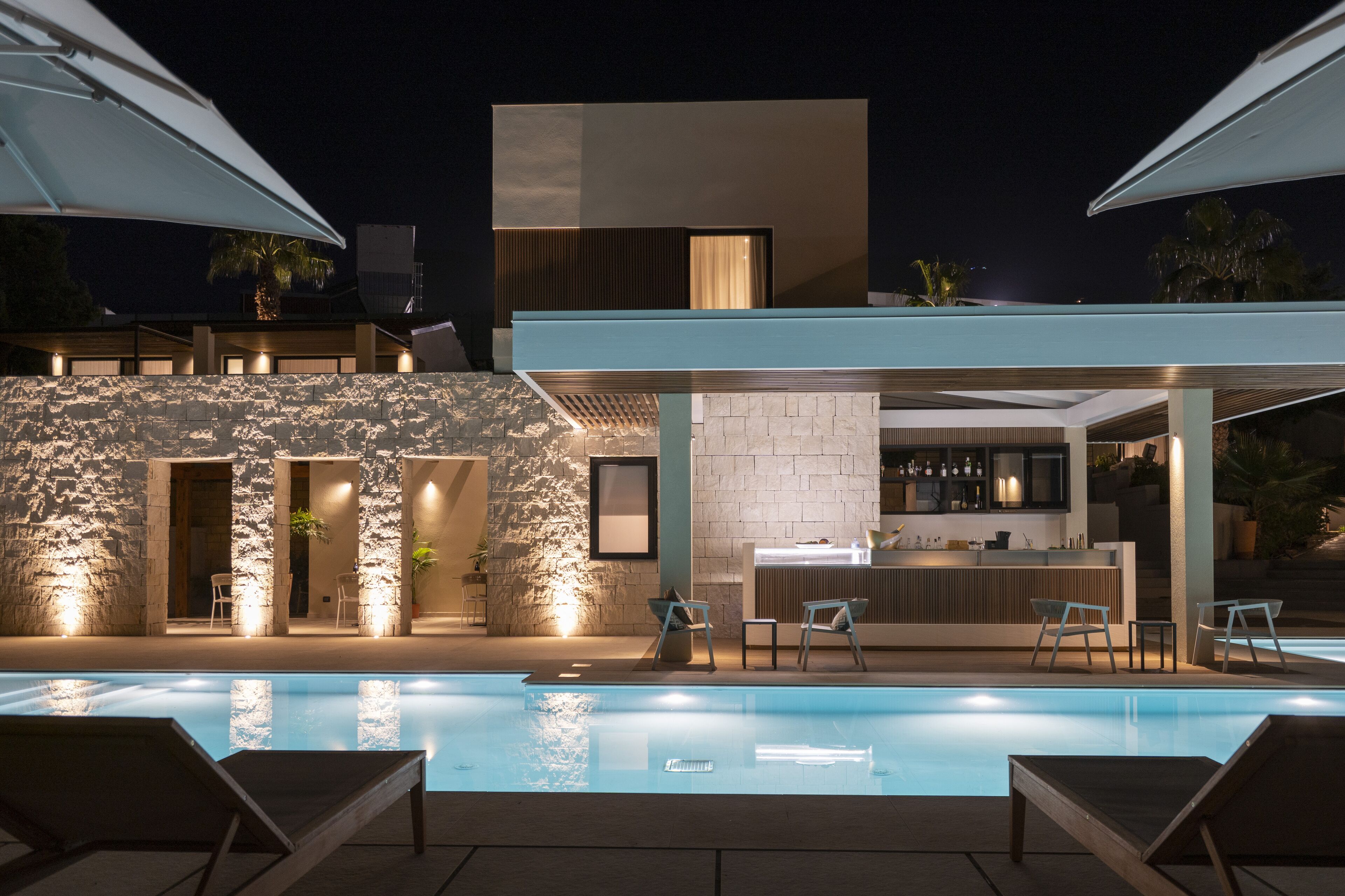 Uma área de piscina moderna ao ar livre, com espreguiçadeiras, um bar e um muro de pedra.