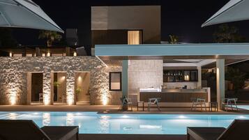 Uma área de piscina moderna ao ar livre, com espreguiçadeiras, um bar e um muro de pedra.