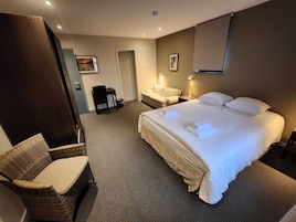 Quarto de hotel com uma cama grande, uma cadeira, uma mesa e uma porta.