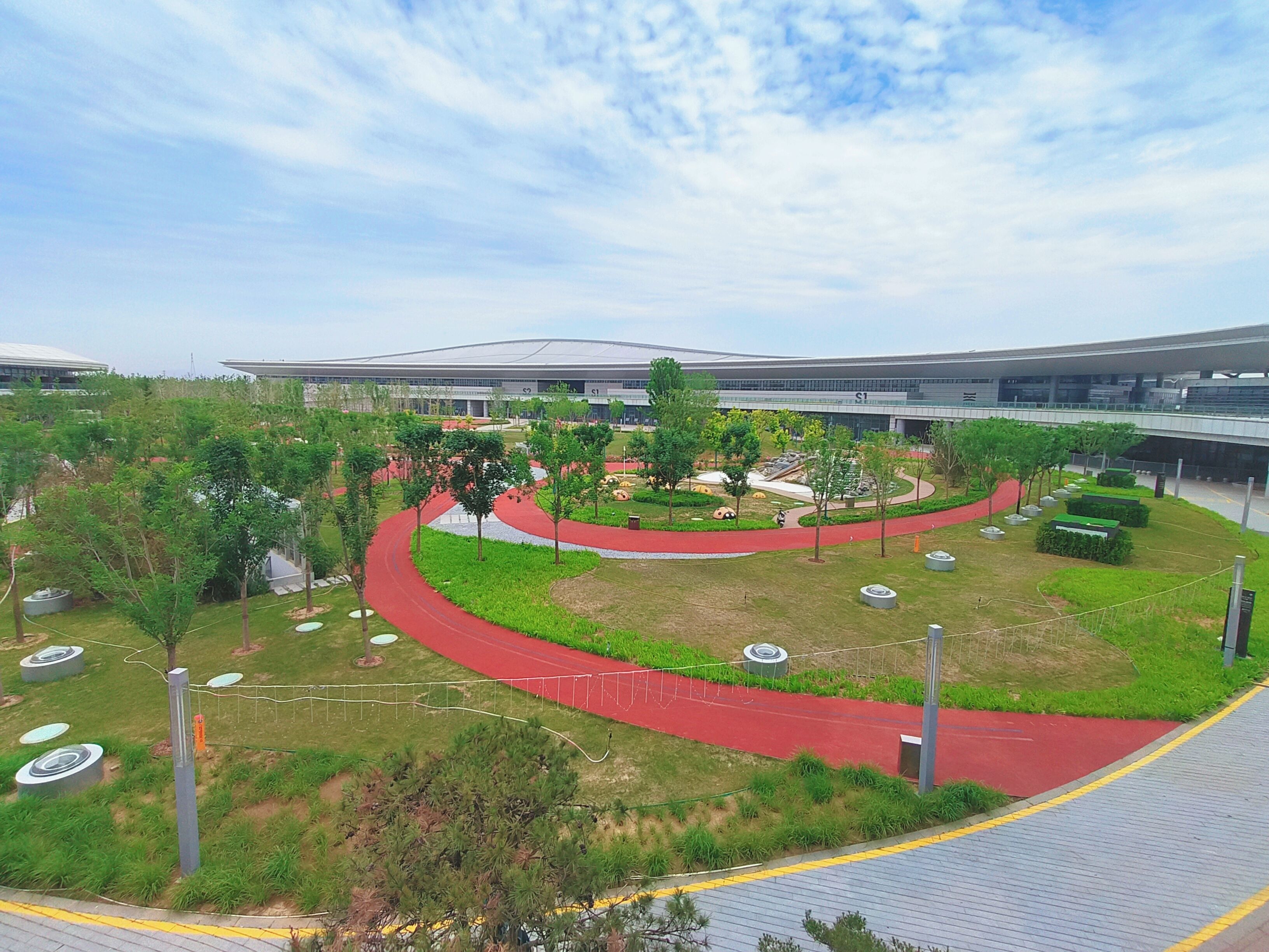 Um edifício moderno com um caminho curvo vermelho, paisagismo verde e céu limpo.